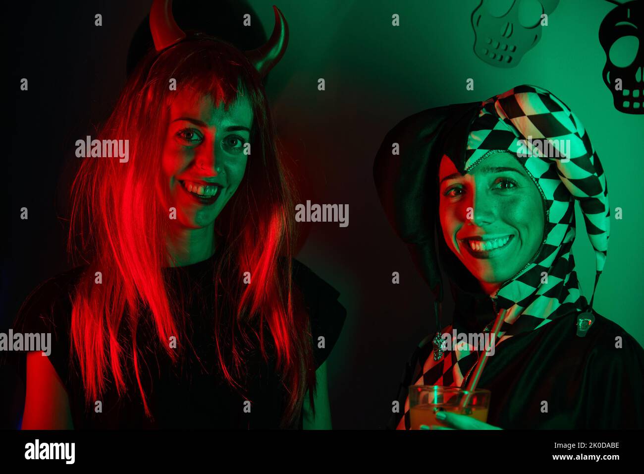 Two women dressed as a harlequin and devil smiling at a Halloween party ...
