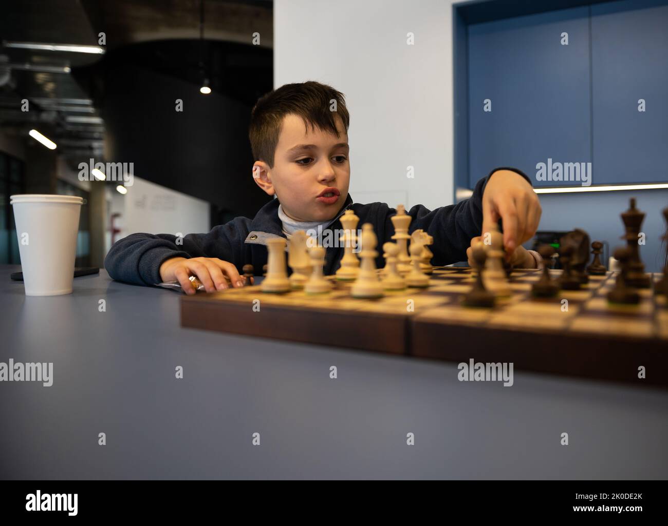 Intellectual schoolboy plays chess, moves a chess piece on checkerboard ...