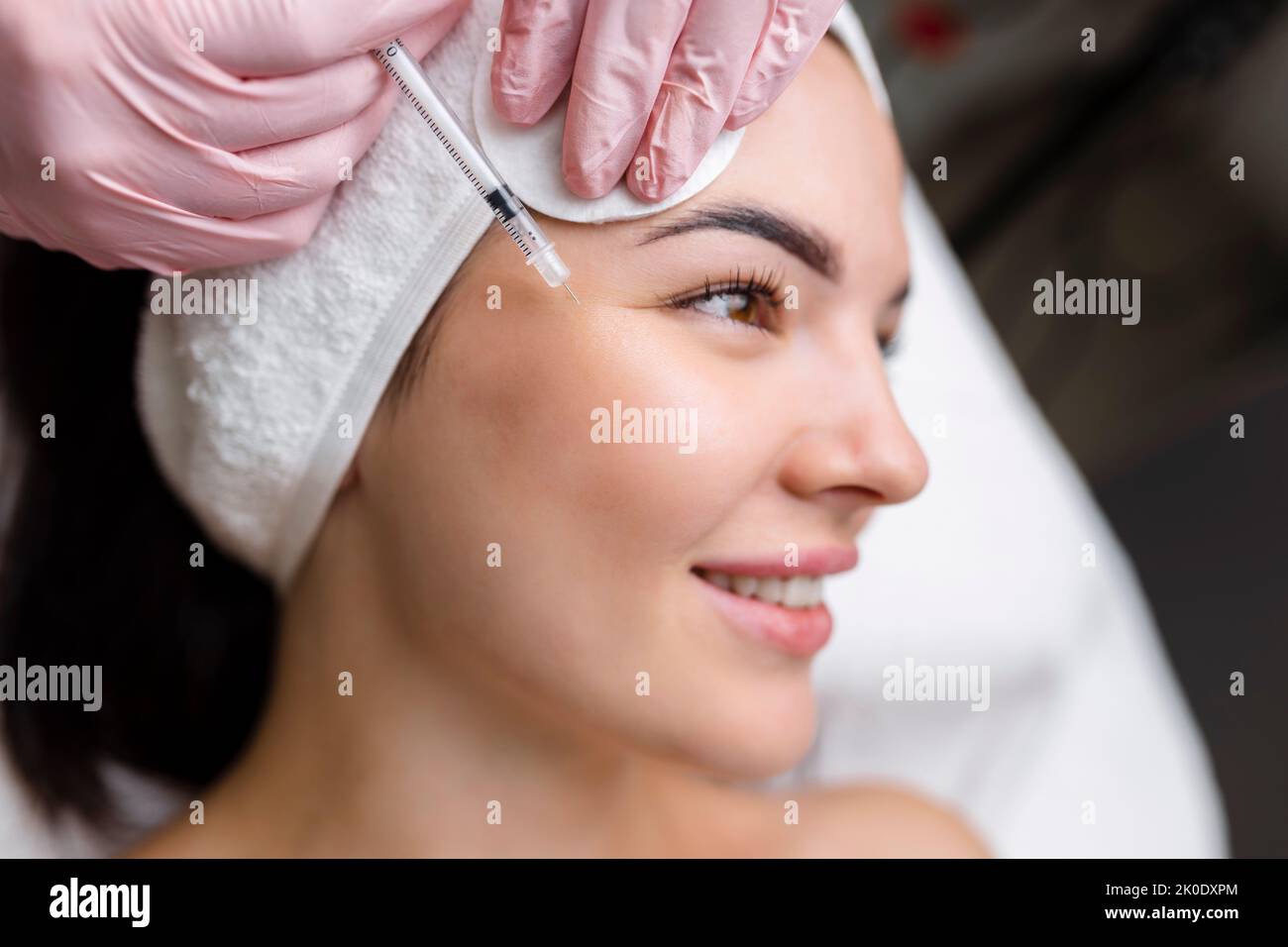 Close up of hands of young cosmetologist injecting botox in female face ...