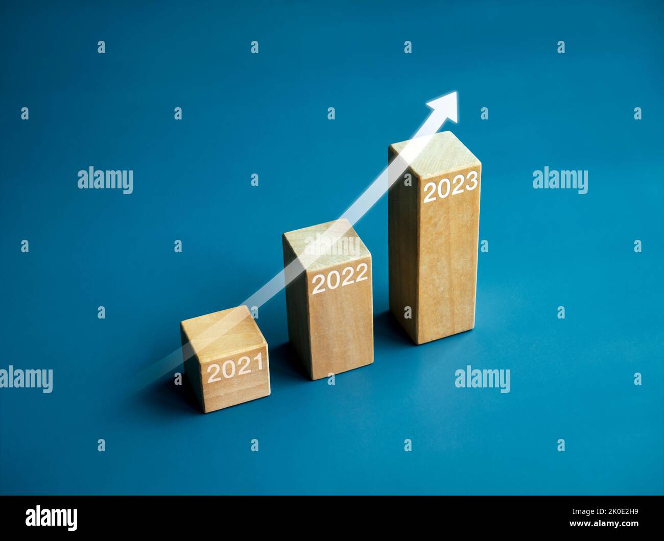 Shining rise up arrow on wooden cube blocks, bar graph chart steps from year 2021 to 2023 on ...