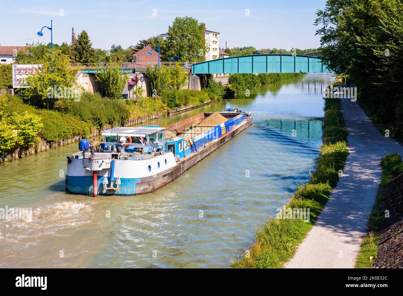 A motorised barge loaded with gravel is sailing on a canal through an ...