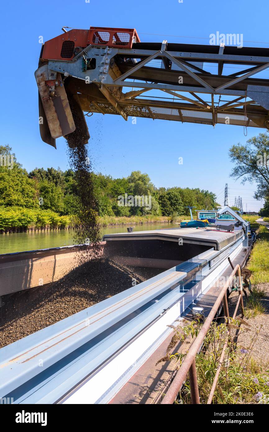 A motorised barge moored on a canal is being loaded with gravel at a ...
