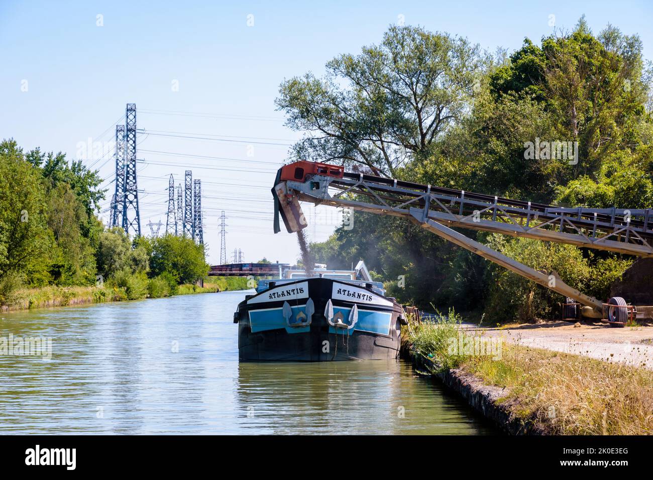 A motorised barge moored on a canal is being loaded with gravel at a ...