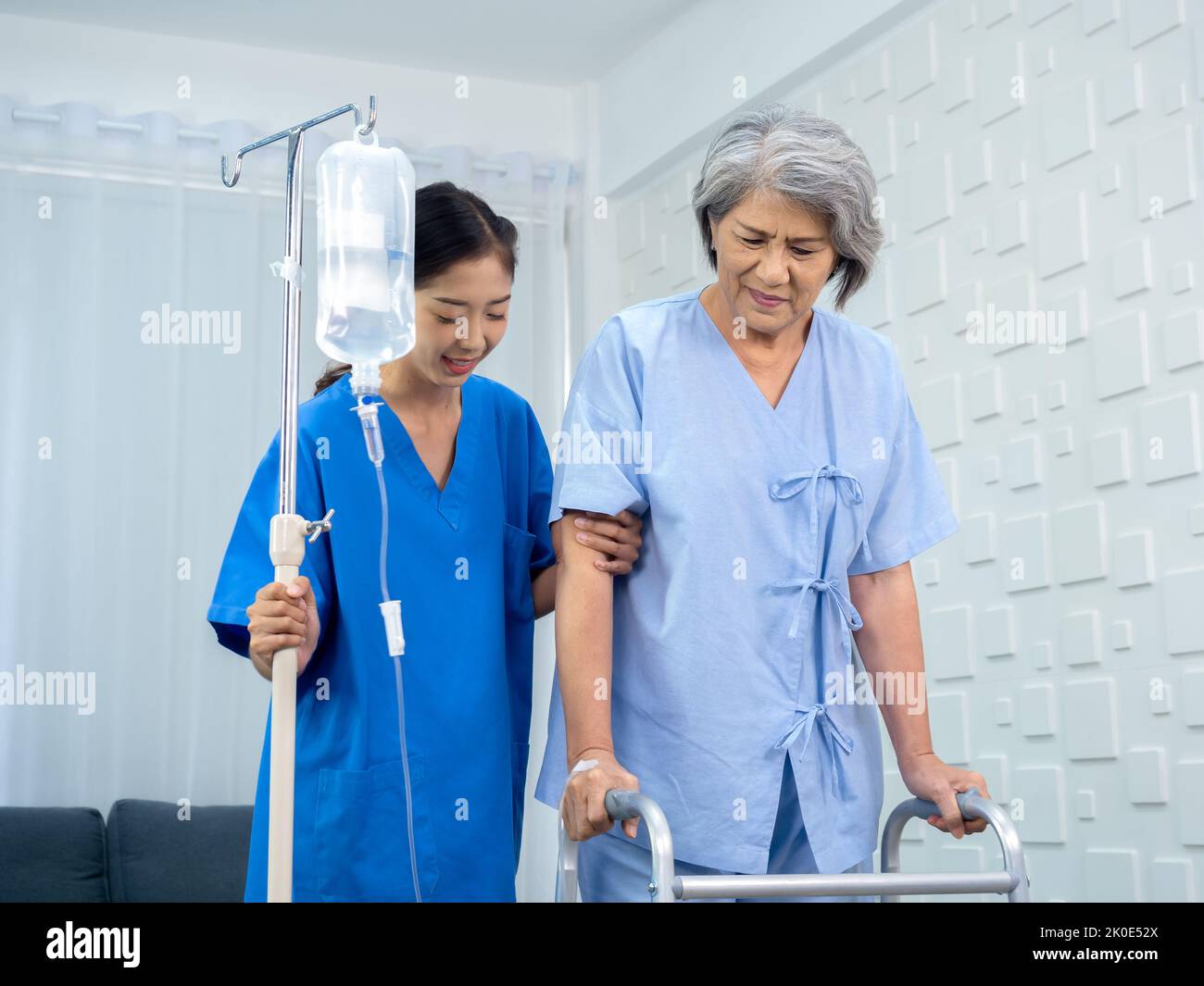 Elderly Asian woman patient trying to walk on walking frame held and ...