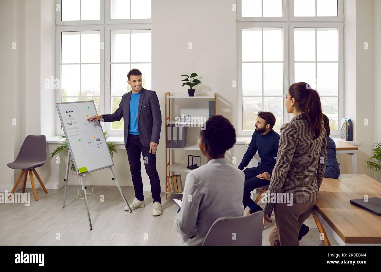 Joyful man makes presentation on whiteboard and explains work strategy ...