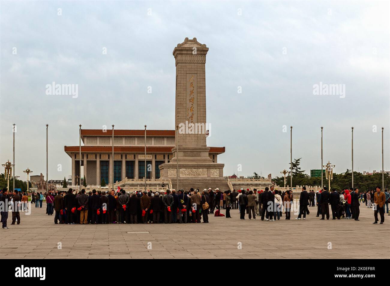Tourists holding red caps stand in front of the ten-storey obelisk ...