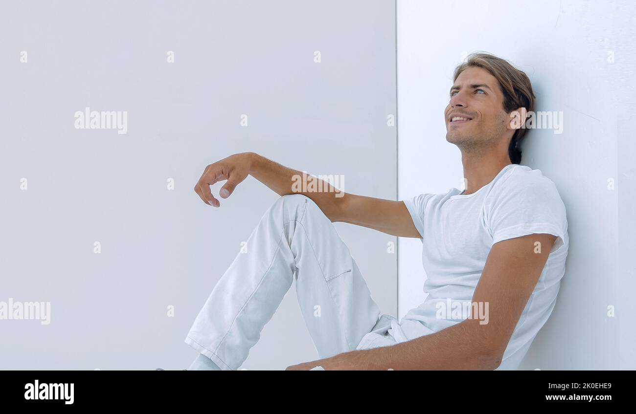 dreamy young man sitting beside a white wall Stock Photo - Alamy