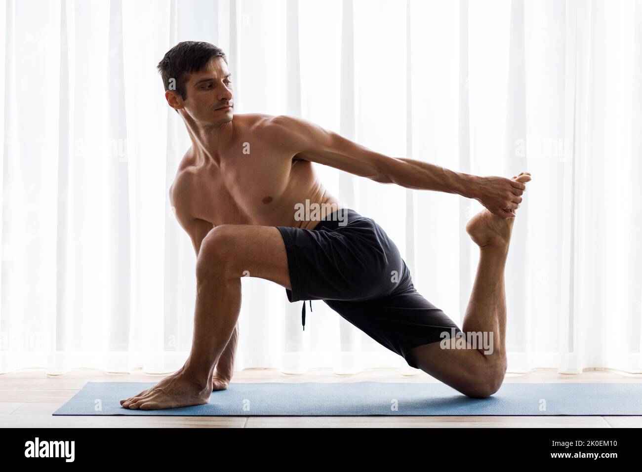 Young sporty man doing stretching legs on yoga mat during morning ...