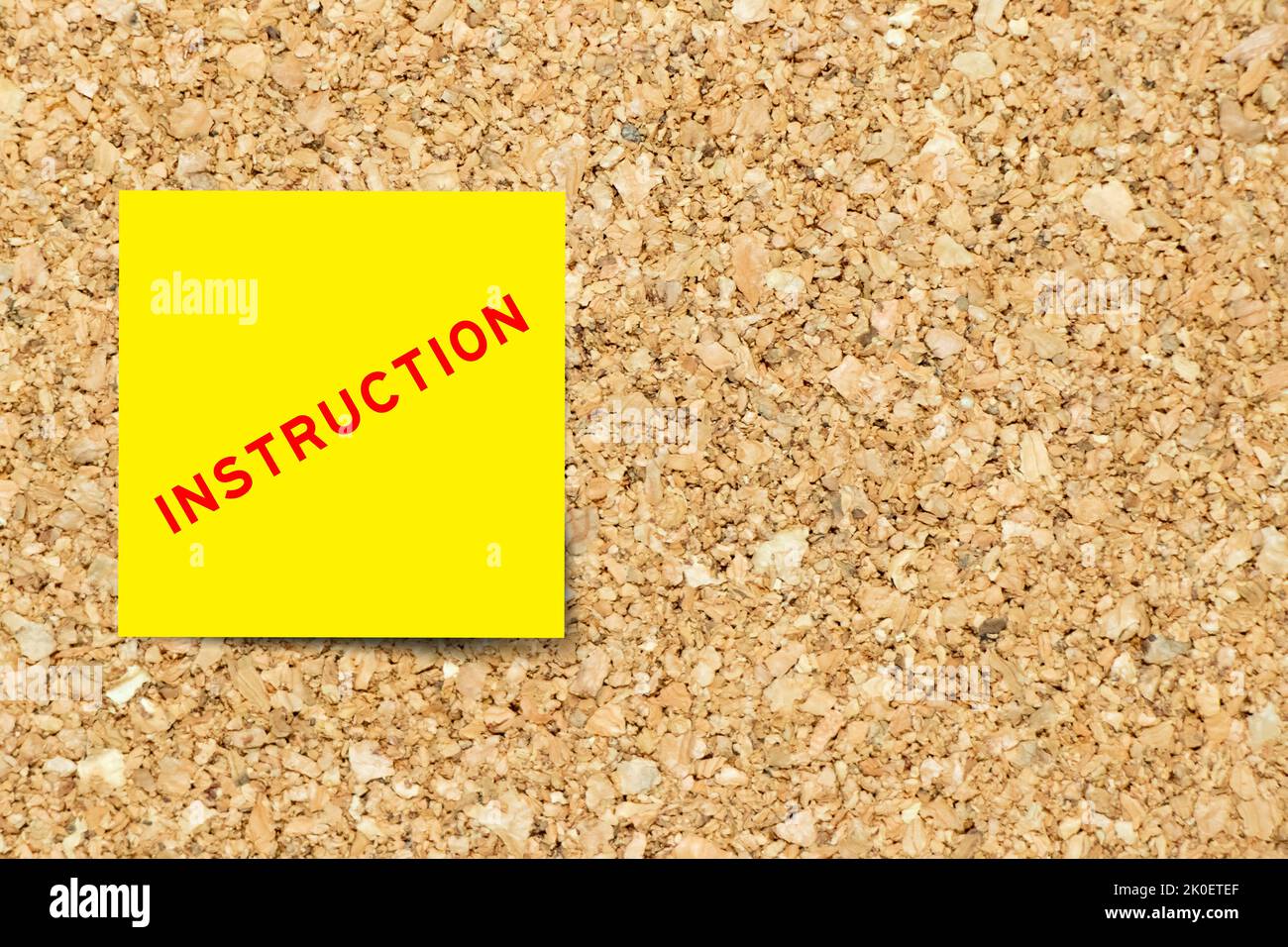 Yellow note paper with word instruction on cork board background with ...