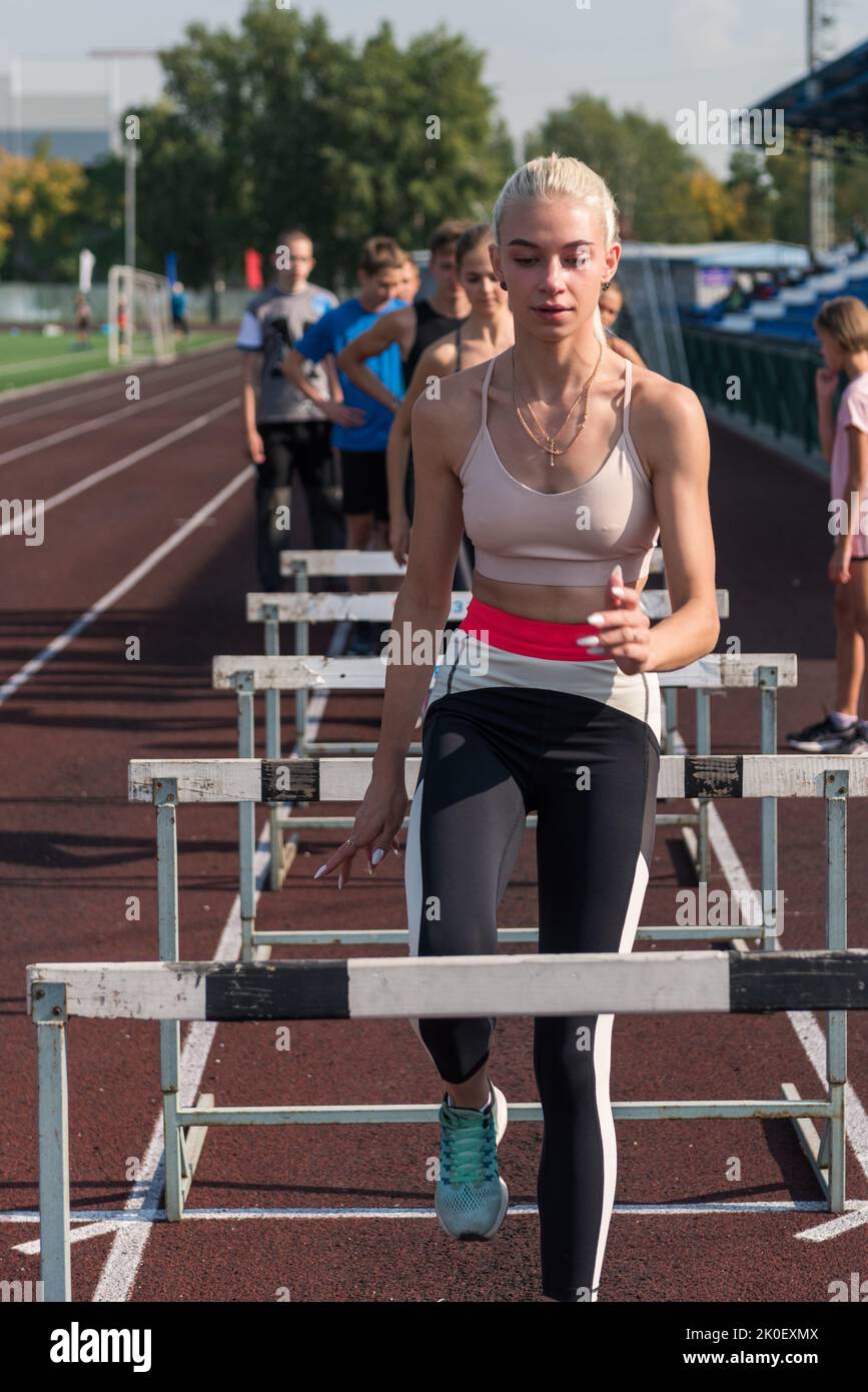 Young woman athlete runnner is exercising hurdles at the stadium ...