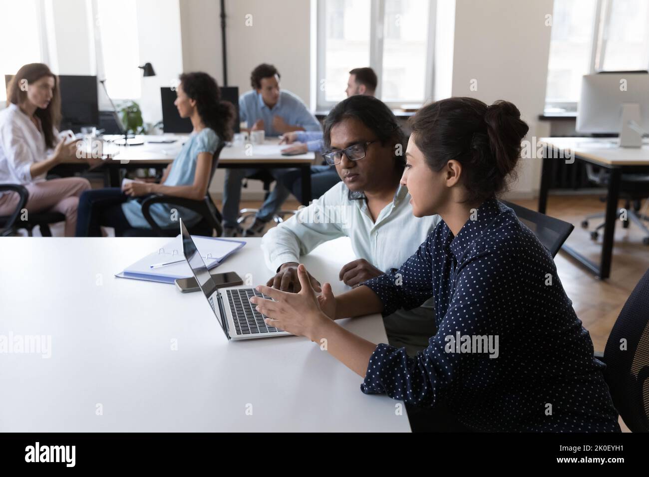 Two serious Indian colleagues talking at work table, sharing laptop ...