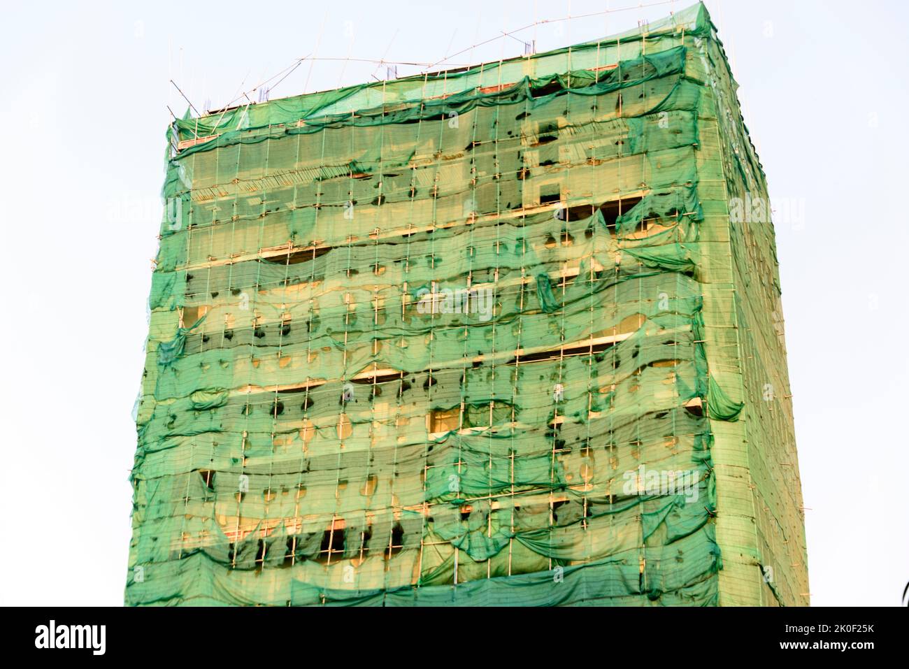 Tall building with bamboo scaffolding, and covered in tattered ripped ...