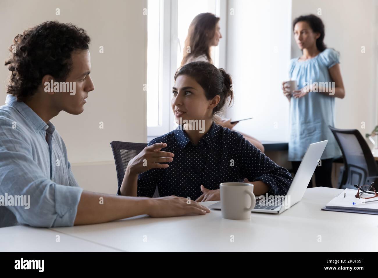 Two young multiethnic employees talking at workplace, discussing ...