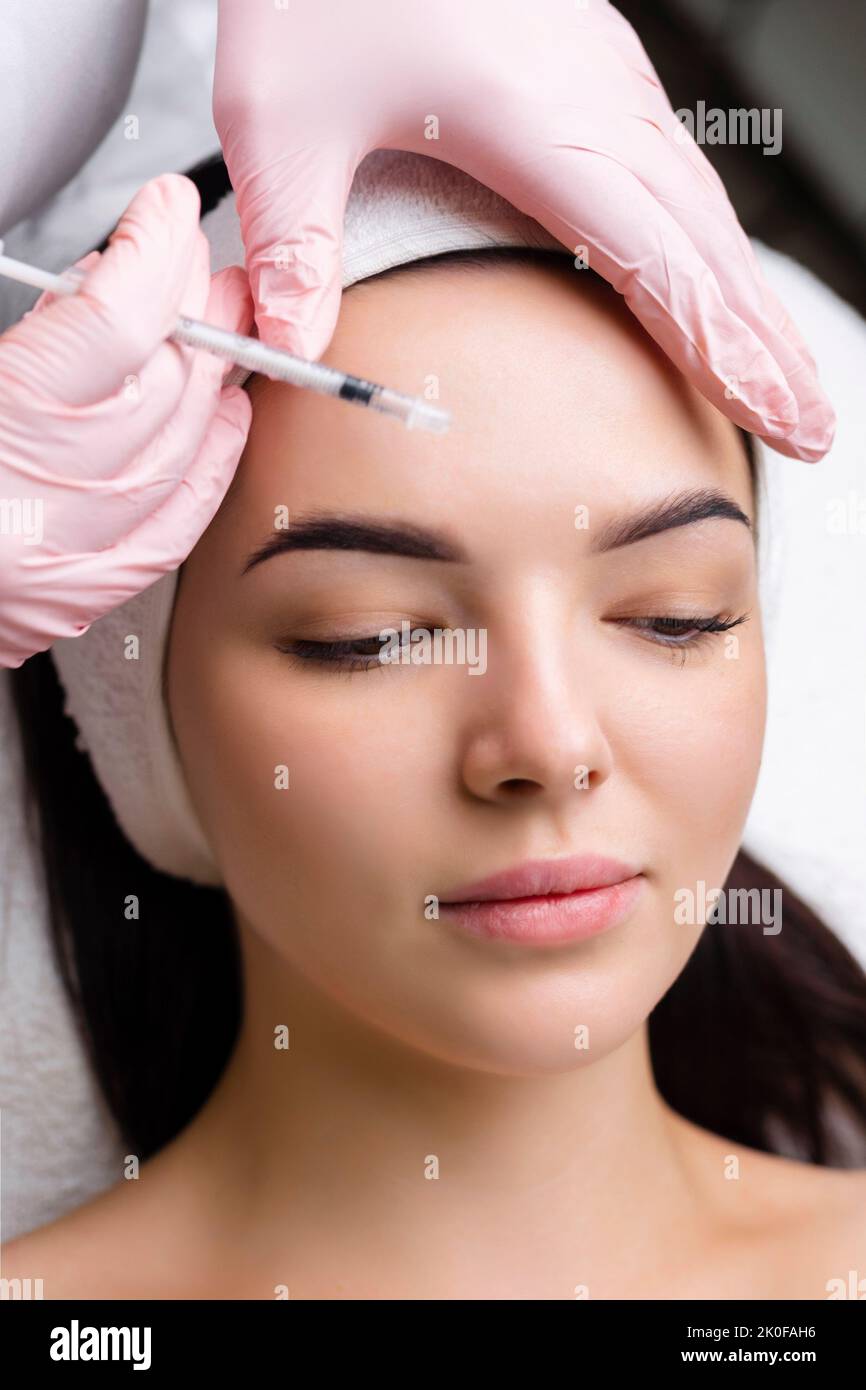 Close up of hands of young cosmetologist injecting botox in female face ...