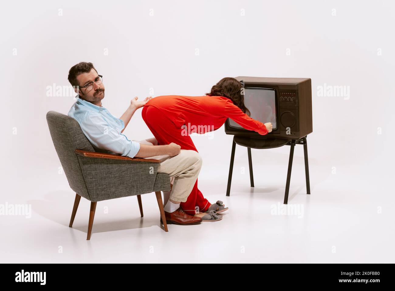 Portrait of woman in red pyjama turning off TV in front of her husband ...