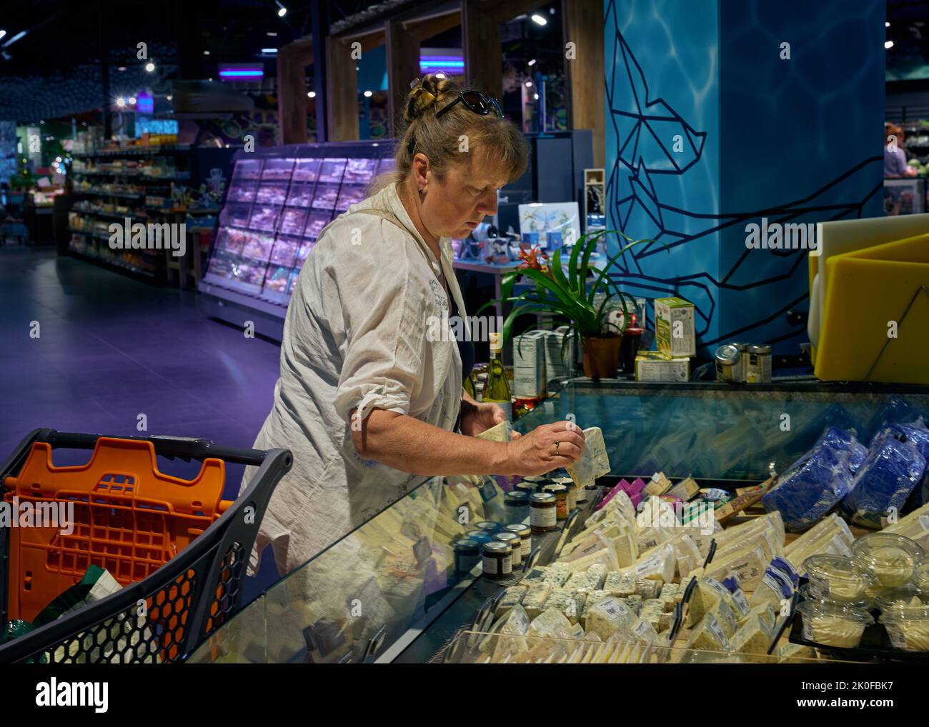 Adult mature pretty woman chooses cheese from a shelf in a supermarket ...