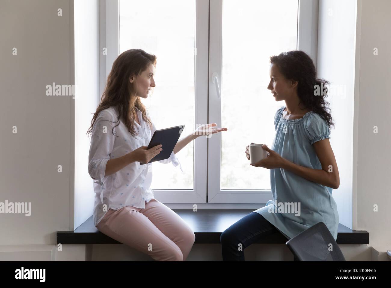 Two diverse coworkers women sitting at office window Stock Photo - Alamy