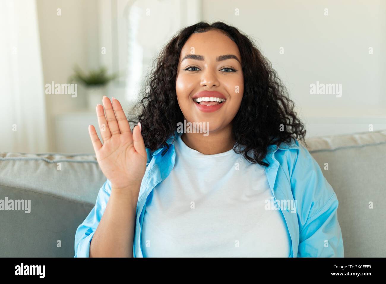 Happy Black Lady Waving Hello Sitting On Sofa At Home Stock Photo - Alamy