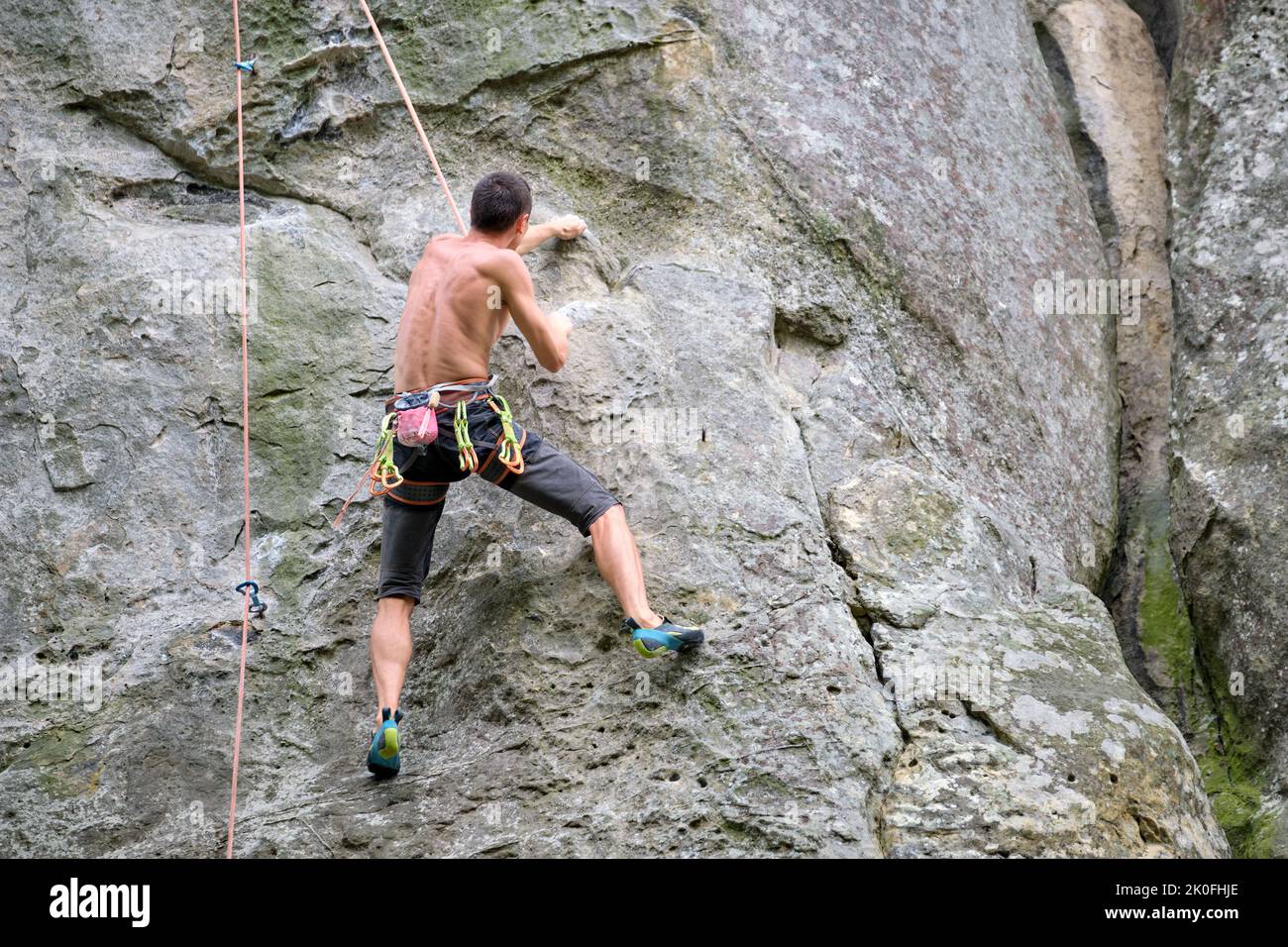 Determined climber clambering up steep wall of rocky mountain ...