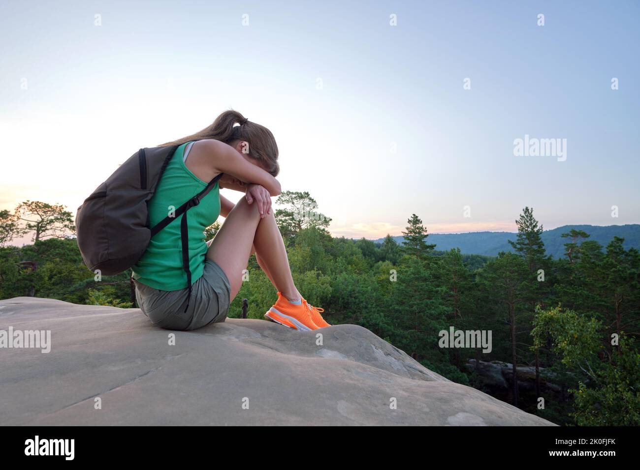 Lonely sad hiker woman sitting alone on rocky mountain top on warm ...