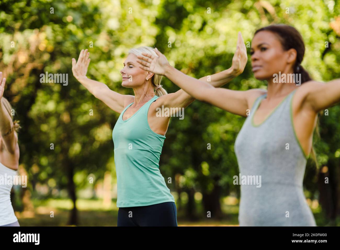 Multiracial women doing exercise during yoga practice in summer park ...