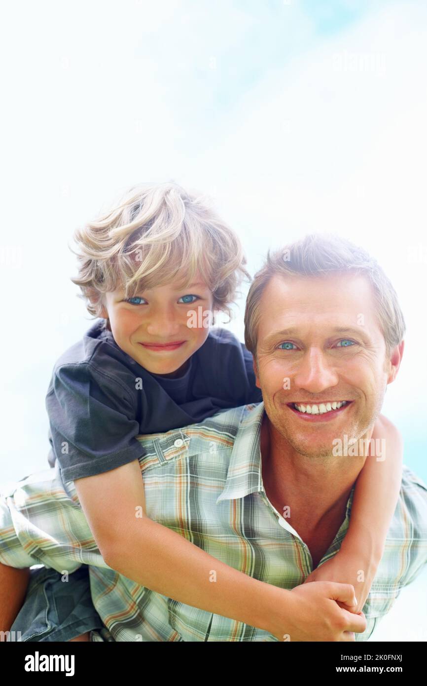 Smiling father giving his son piggy back ride against sky. Portrait of a smiling father giving ...