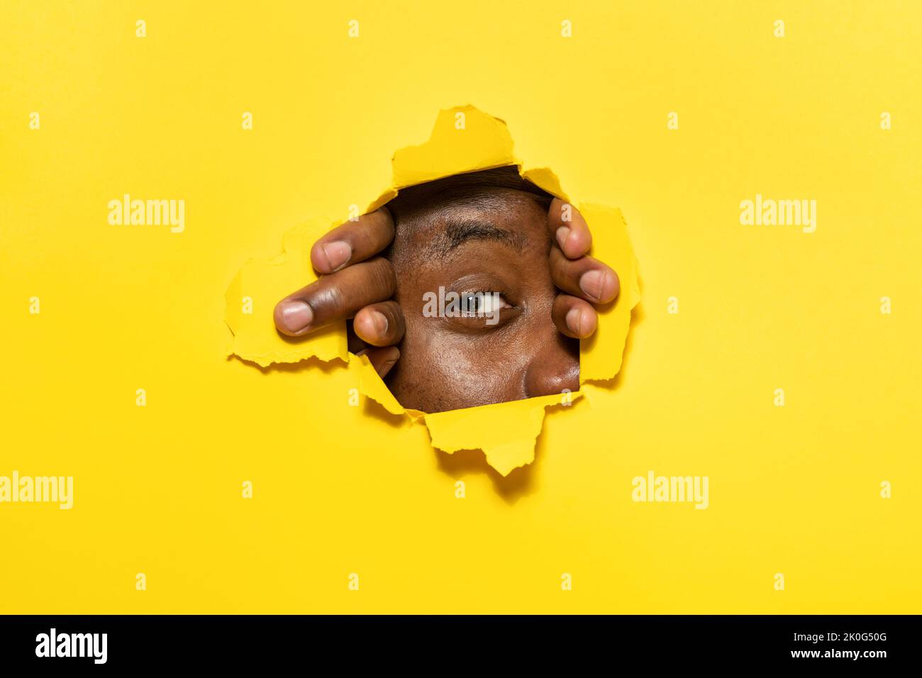 Young african american man peeking out of a hole in yellow paper ...