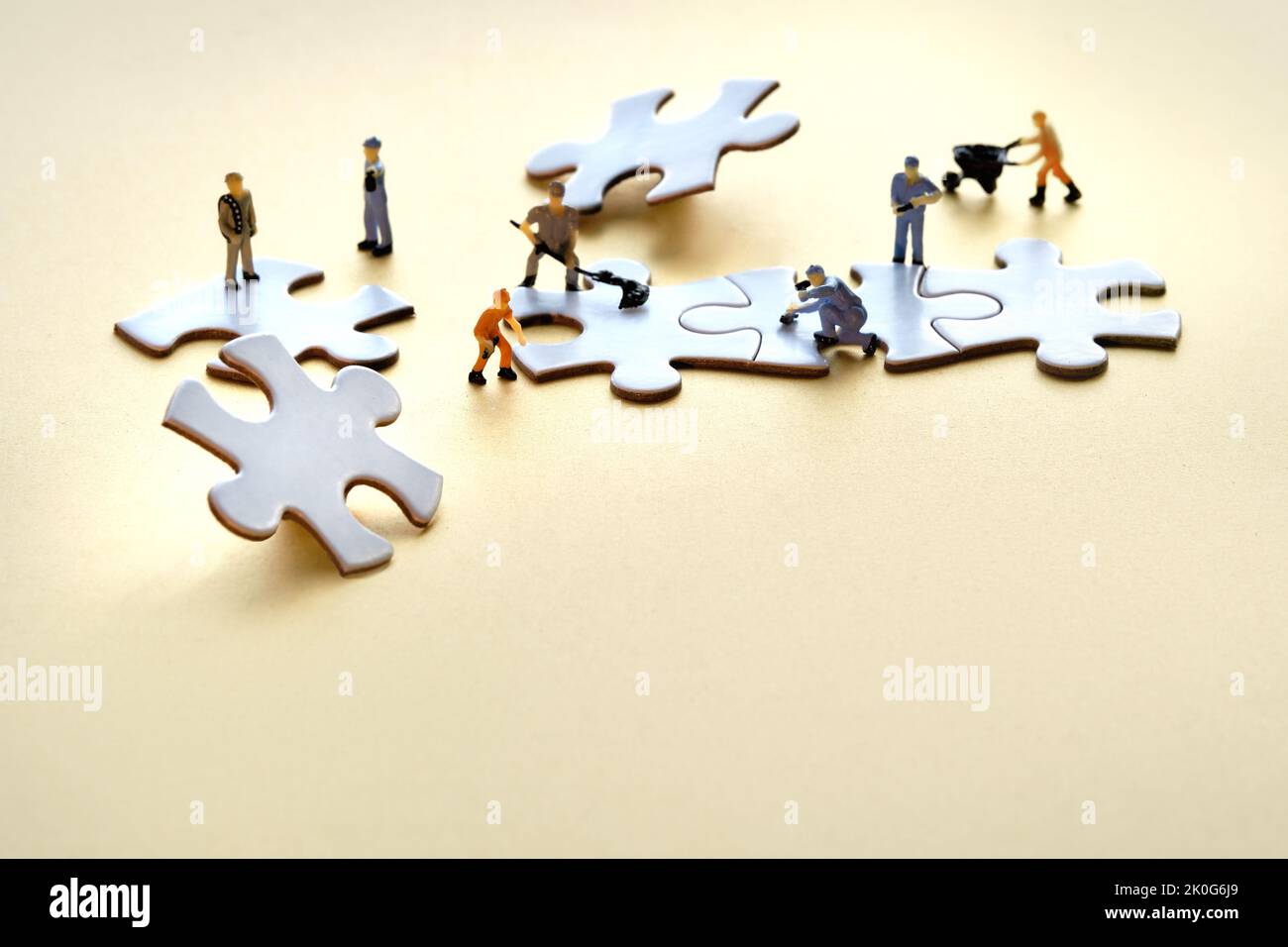 Team of tiny worker miniature figures on linked jigsaw puzzle pieces on ...