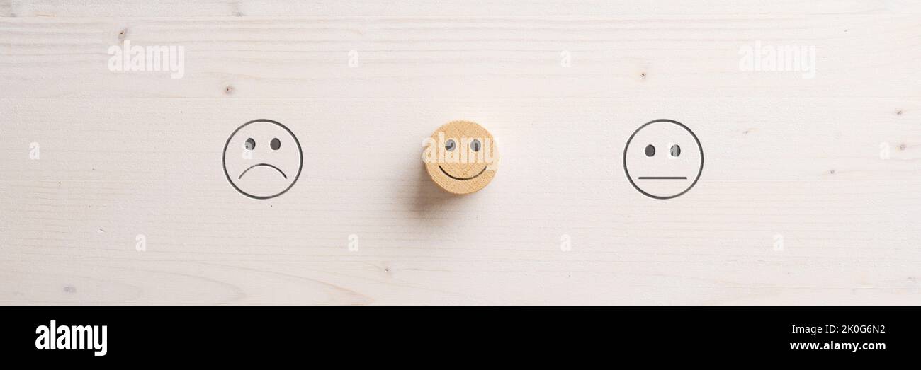 Sad and neutral emoji face symbols cut into wooden background and a ...