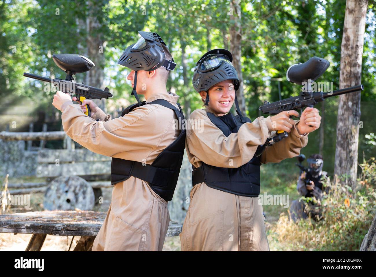 Boy and girl paintball players standing back-to-back and shooting Stock ...