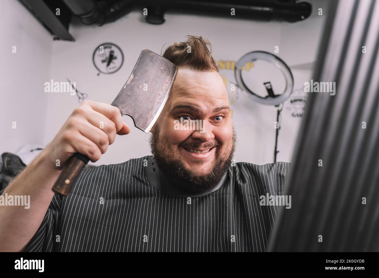 Bearded hipster man shaving his head with an ax looking to the mirror ...