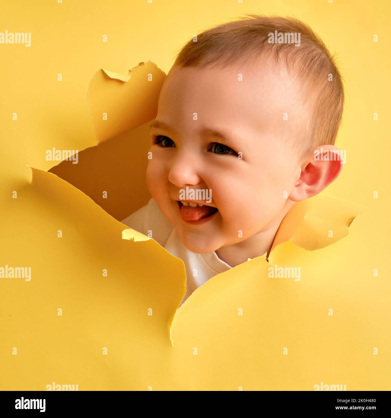 A happy child looks out of a hole in the studio yellow background ...