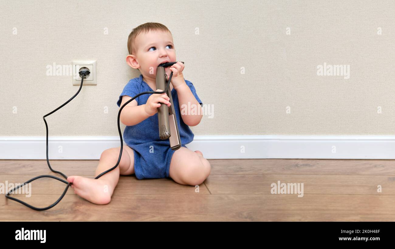 Child boy chewing on the electric wire of a curling iron, copy space ...