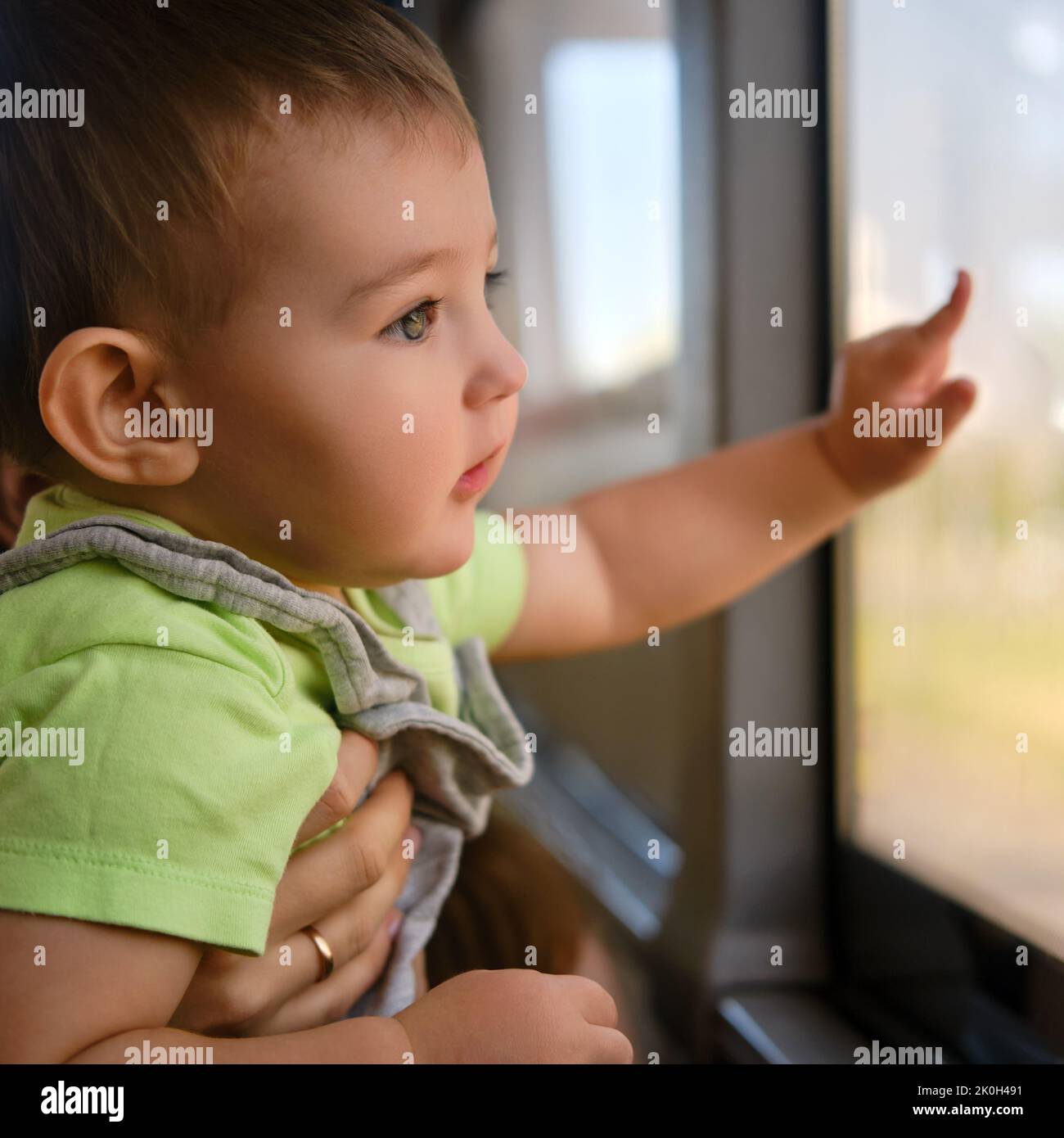 Toddler baby looks out the bus window while sitting in the arms of his ...