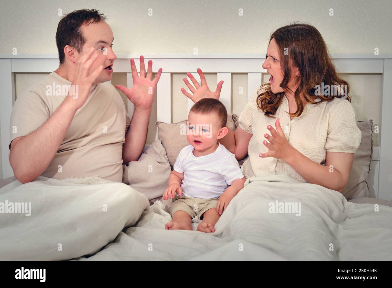 A man and a woman are fighting at a toddler baby on the bed. Father and ...