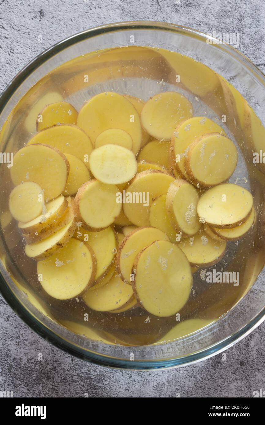 Sliced potatoes soaking, in a glass bowl, in water for cleaning. On a ...