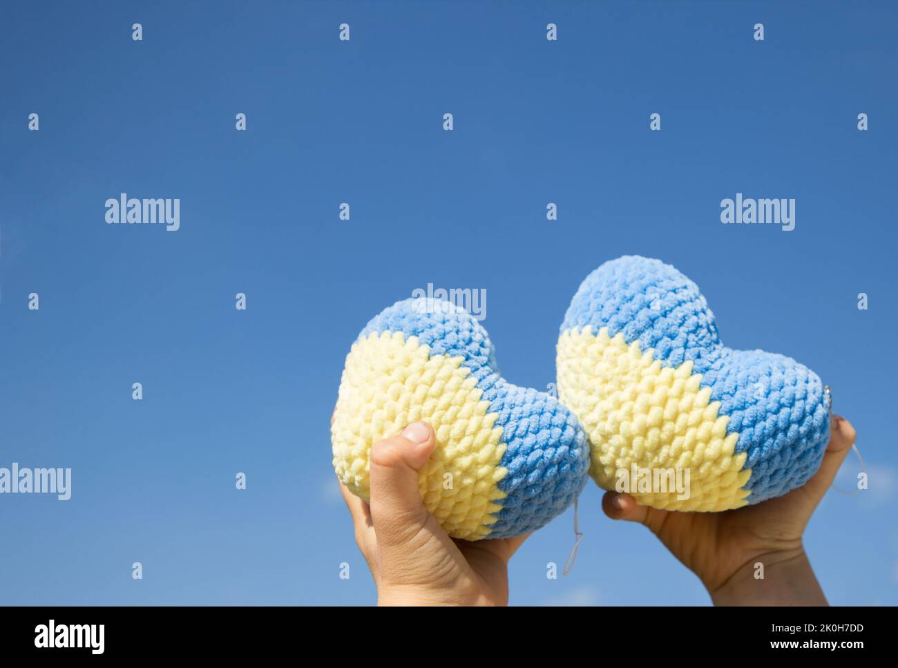children's hands hold two knitted plush yellow-blue hearts against the ...