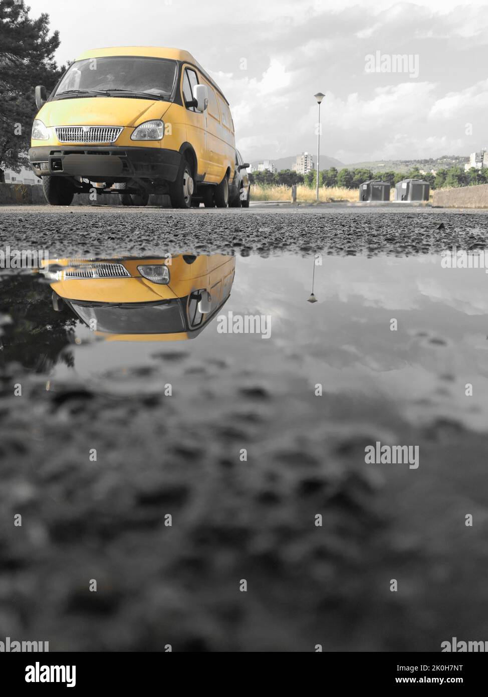 A low-angle shot of a yellow van reflection captured in a water puddle ...