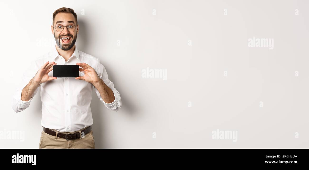 Excited handsome man showing mobile phone screen, looking amazed ...