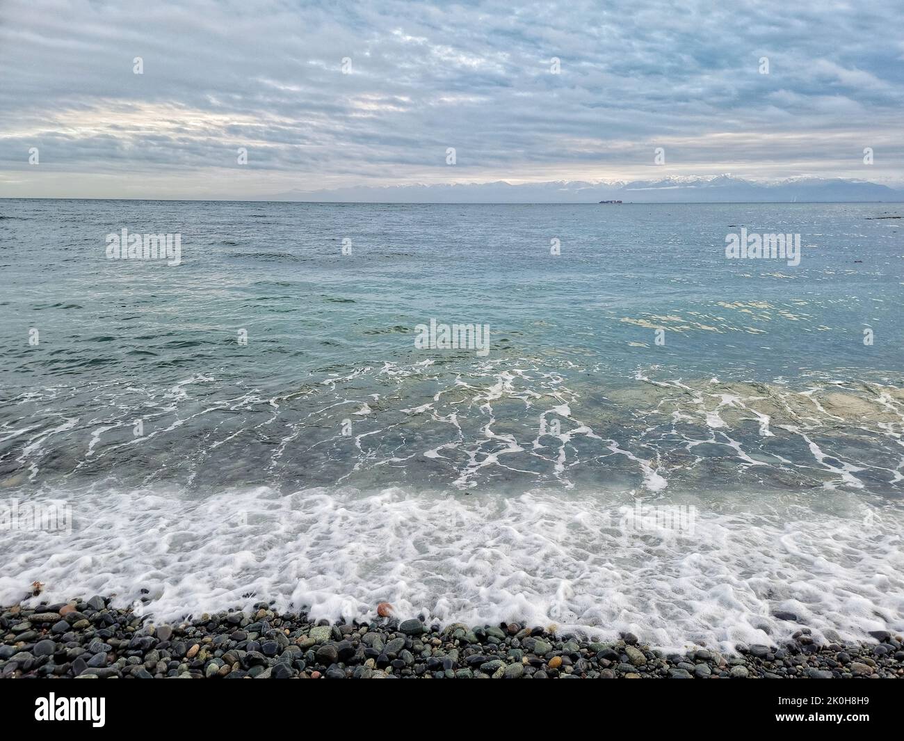 A beautiful seascape with a tide and a pebbled coast under the cloudy ...