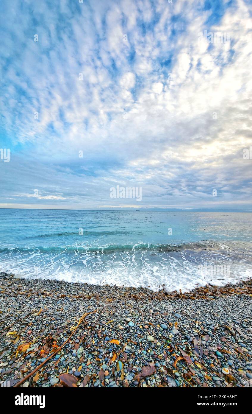 A vertical shot of a beautiful seascape with a tide and a pebbled coast ...
