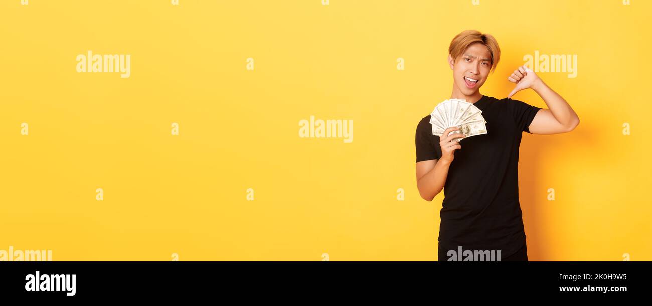 Sassy handsome asian guy pointing finger at cash and looking pleased ...