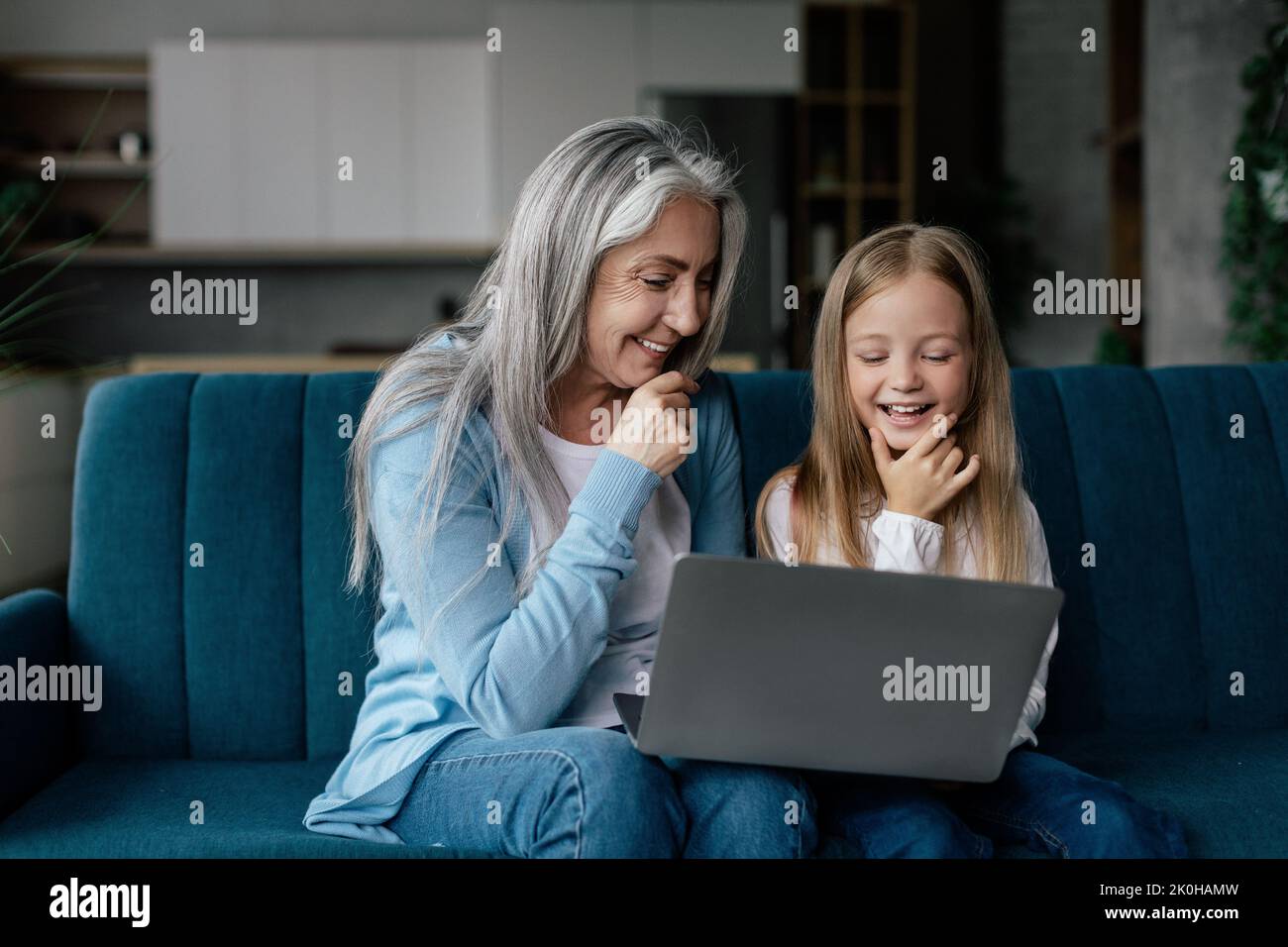 Cheerful caucasian little granddaughter and senior grandma think, watch ...