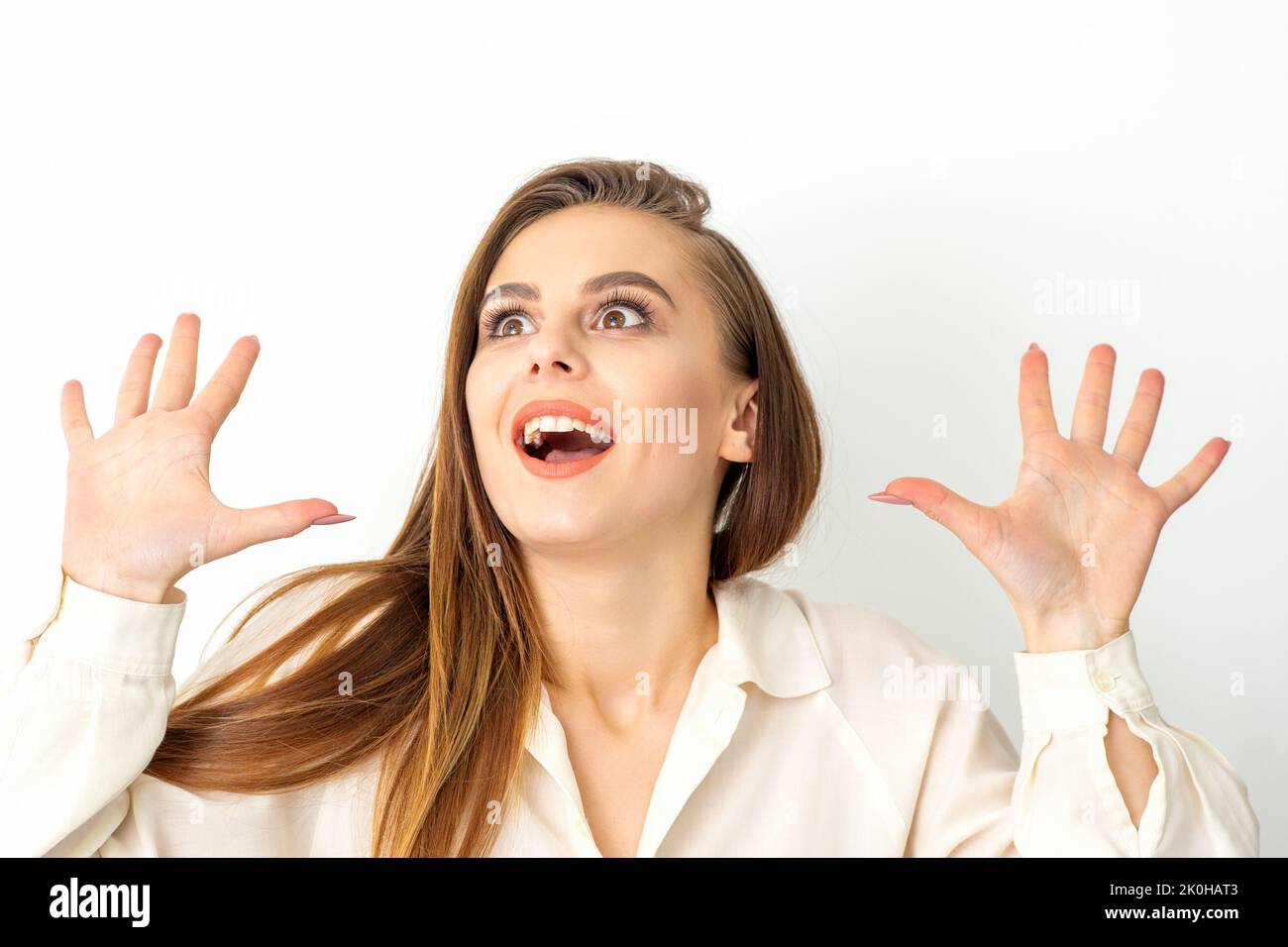 Portrait of young caucasian woman wearing white shirt raises hands and ...