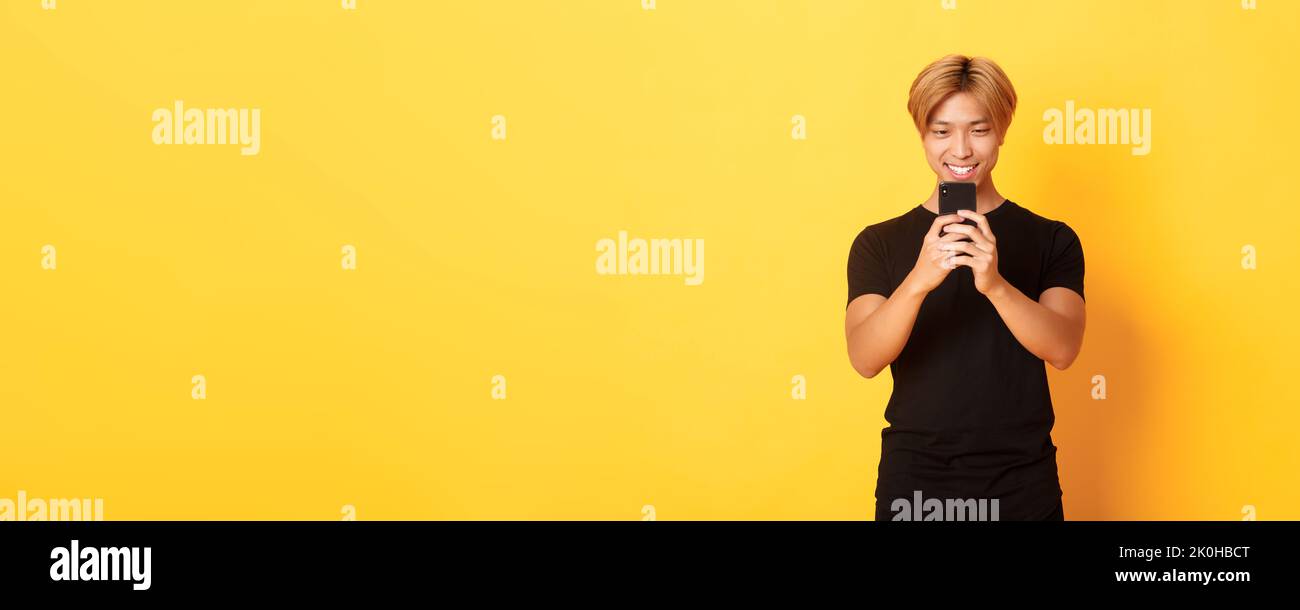 Portrait of handsome stylish asian guy with blond hair, using mobile ...
