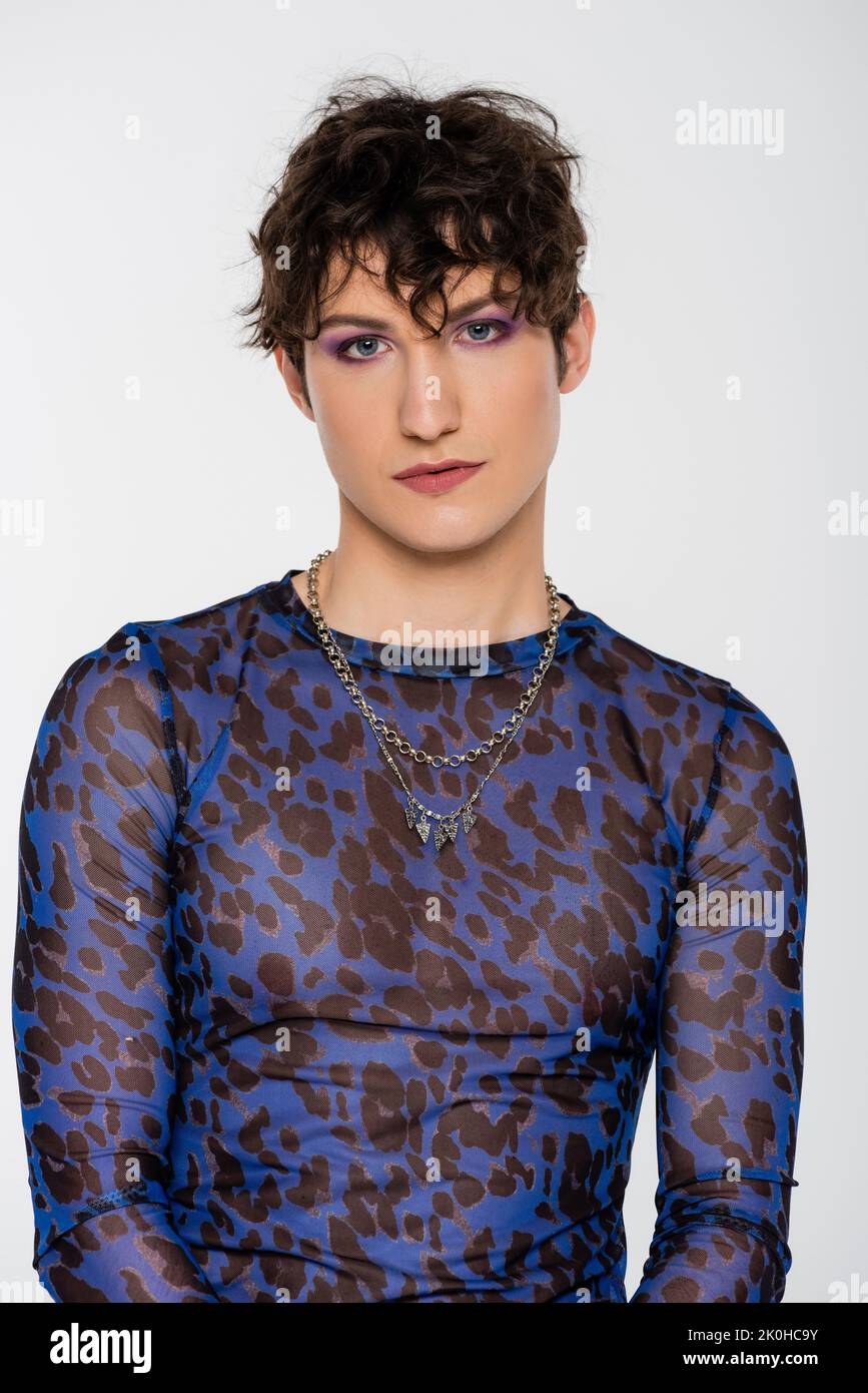 brunette queer model in long sleeve shirt and silver necklaces isolated ...