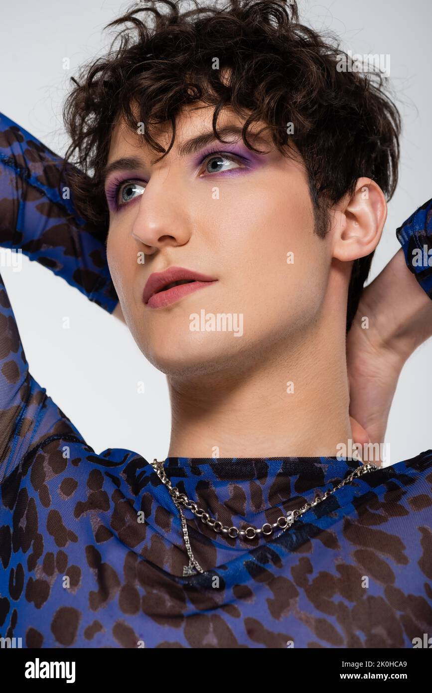 portrait of young queer person with makeup posing with hands behind ...