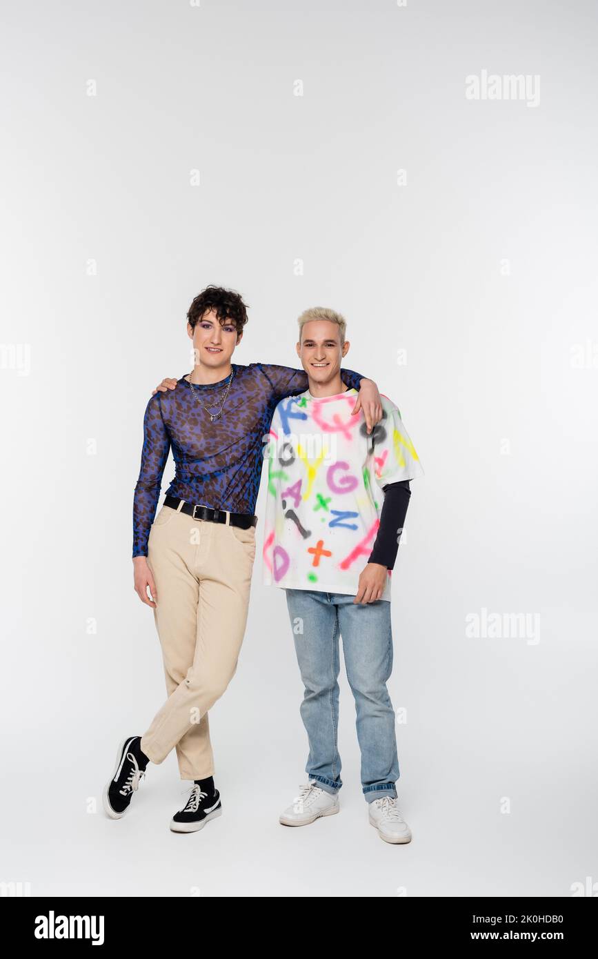 full length of young and joyful queer person with gay man hugging and ...