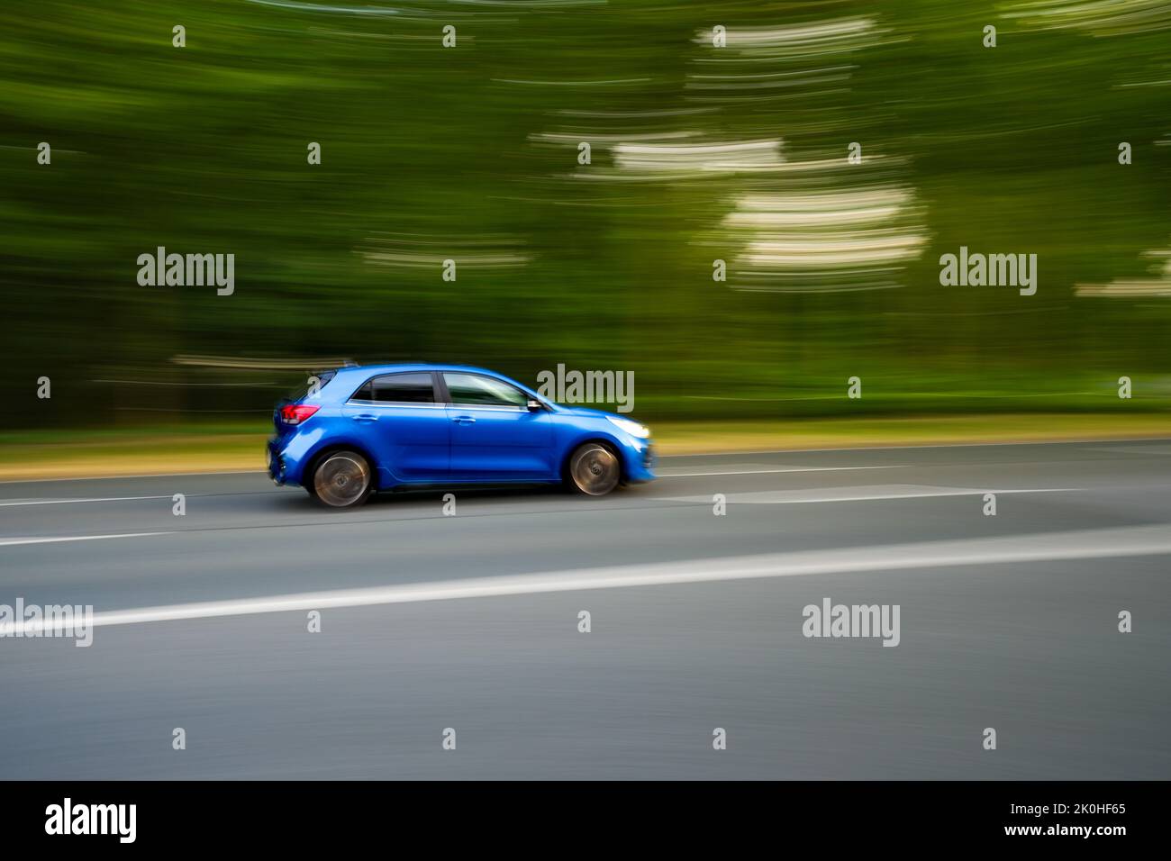 A blue car driving on the road with trees in a motion blur Stock Photo ...
