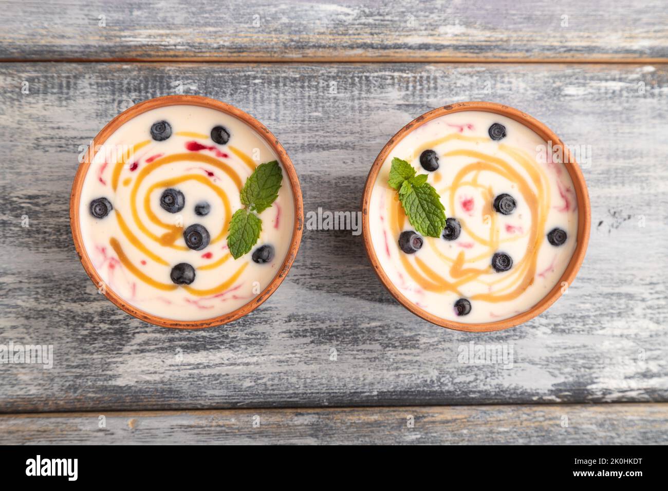 Yoghurt with bilberry and caramel in clay bowl on gray wooden ...